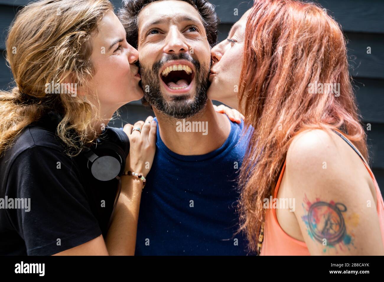 Two young women giving a kiss on each cheek to a young man of different ...