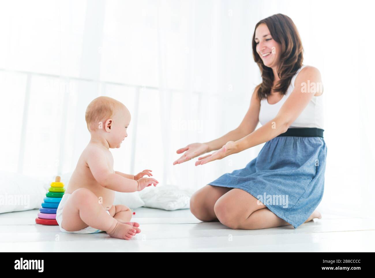 Charming young mother calls to her little baby sitting on the floor in ...
