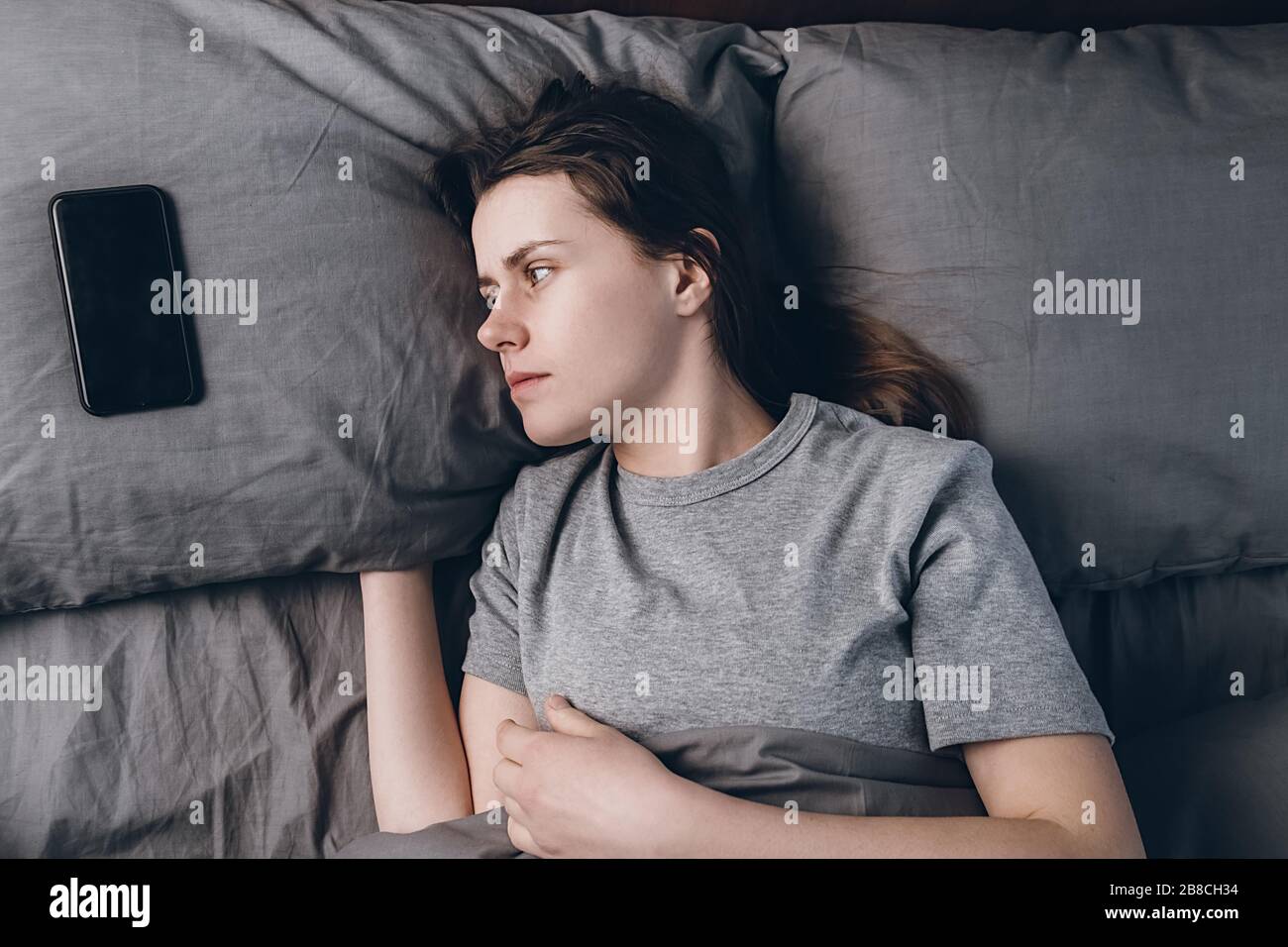 Above top view frightened woman lying in bed looking on smartphone ...