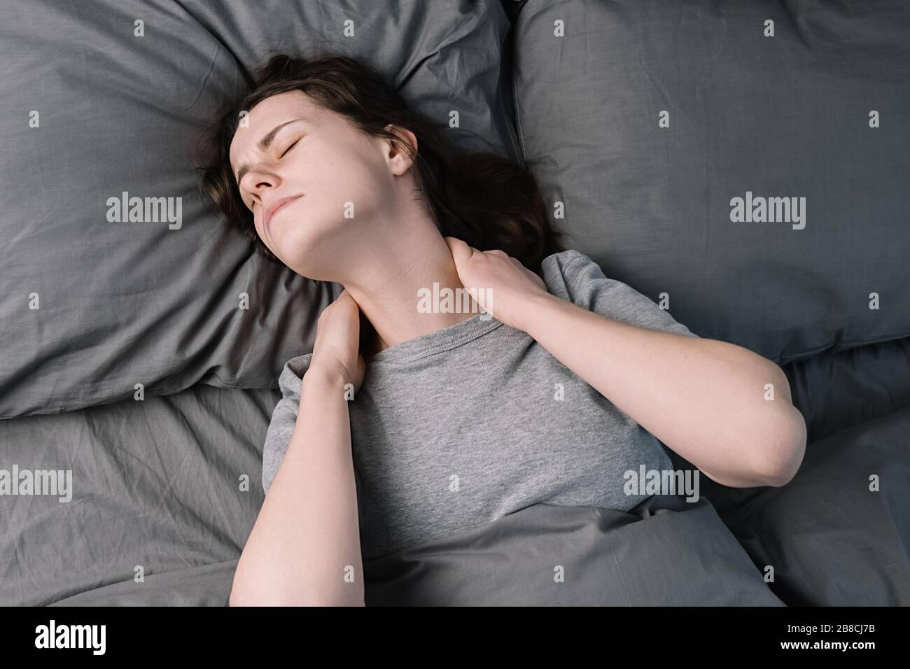 Tired unhappy young woman lying in bed in morning feels pain in neck ...