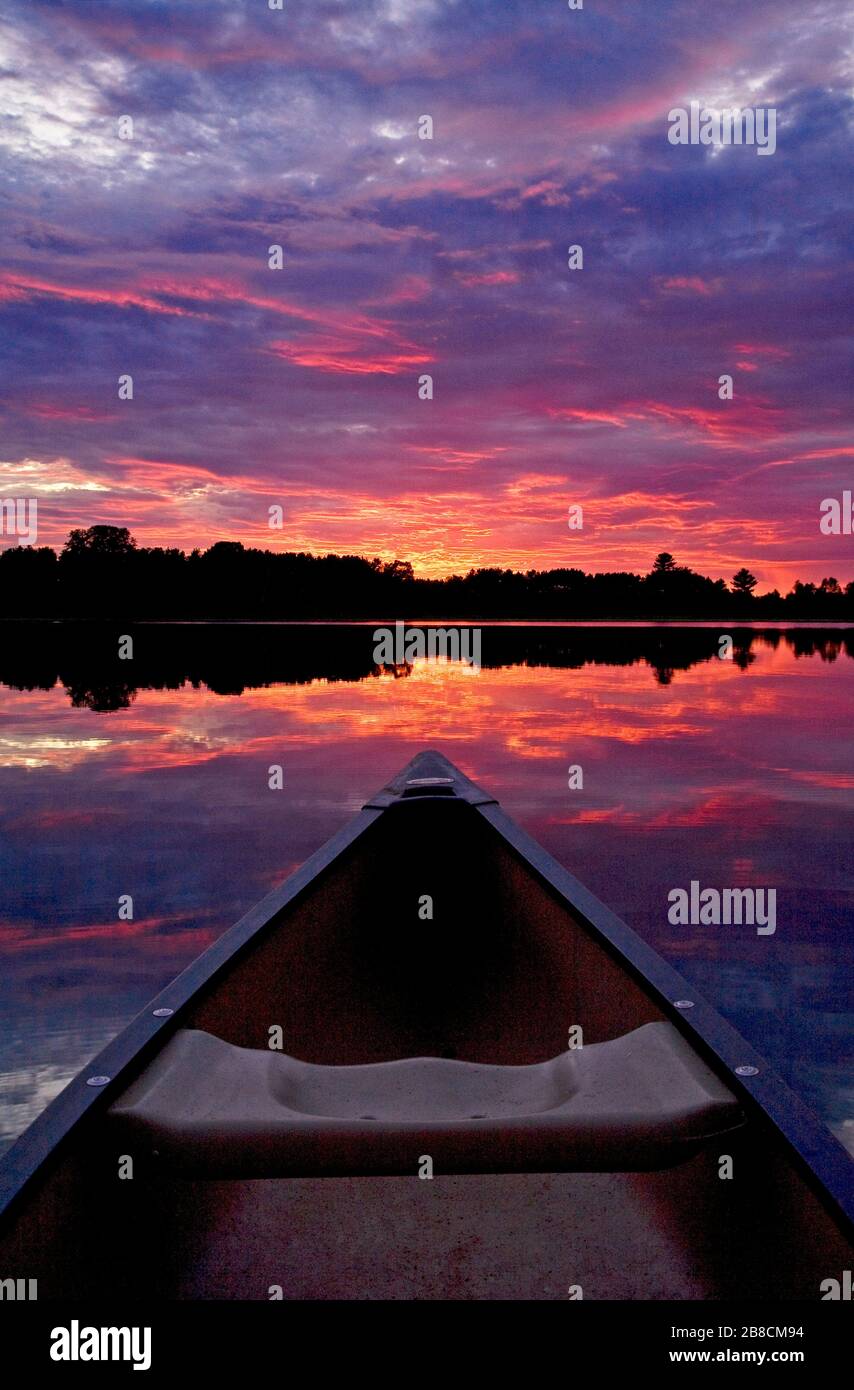 A canoe floats stationary on a quiet lake at sunset in northern ...