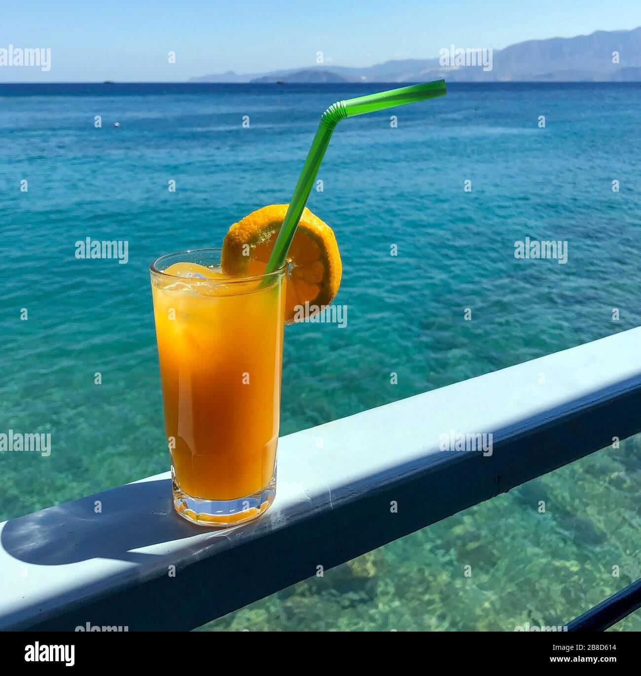 A glass of fresh orange juice with a slice of orange and a straw ...