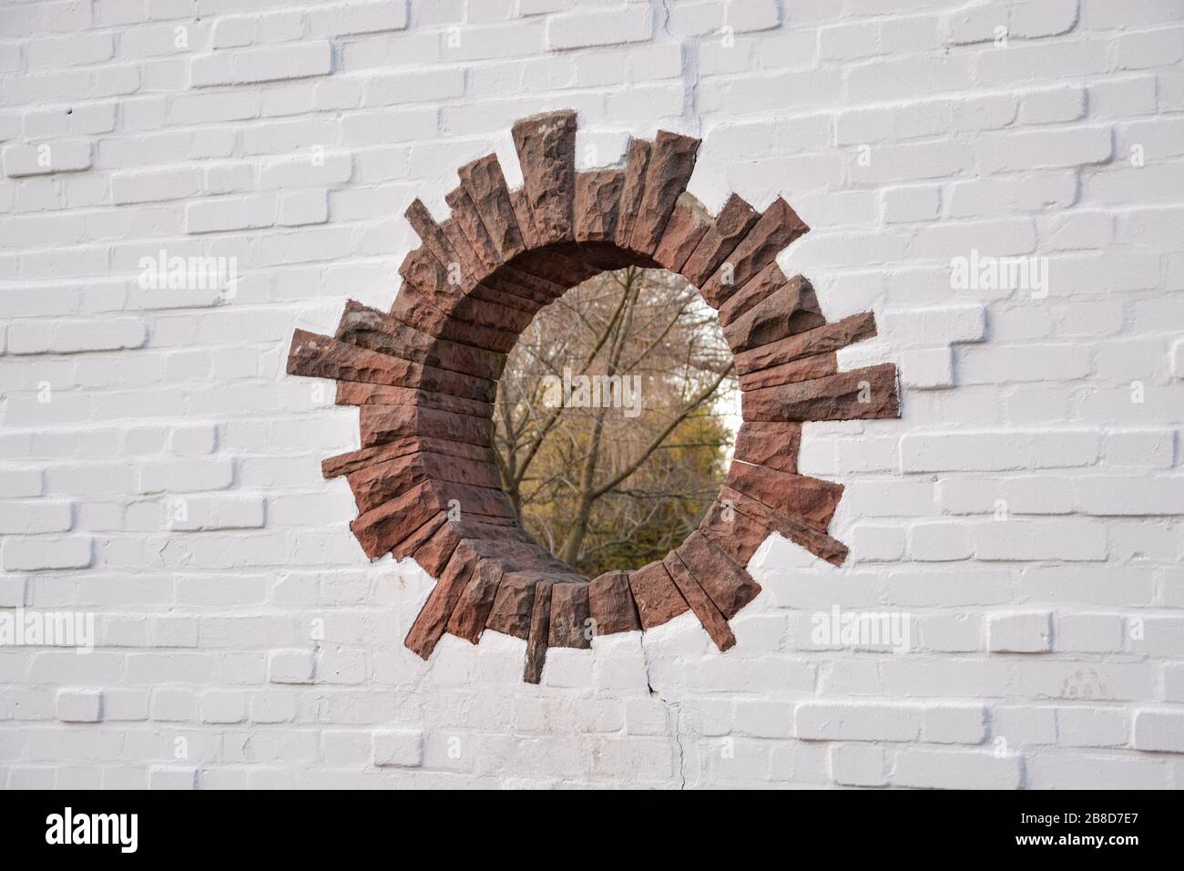 A round hole in a brick wall in a park looks like a portal to another ...