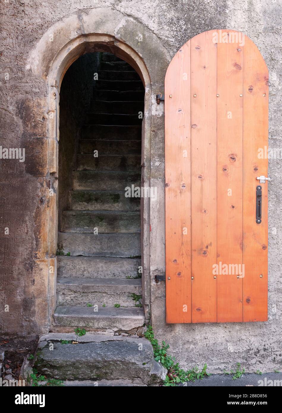 Narrow arch shape stone wall entrance and stairs with a wooden door ...