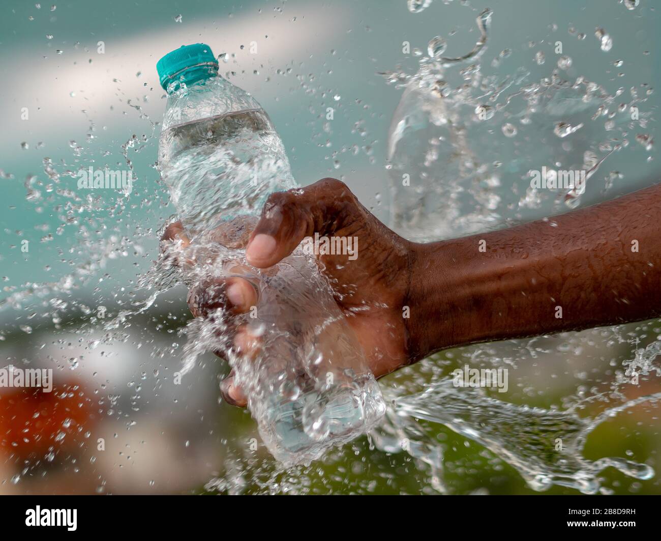 A hand holding a water bottle surrounded by water splash with turquoise ...