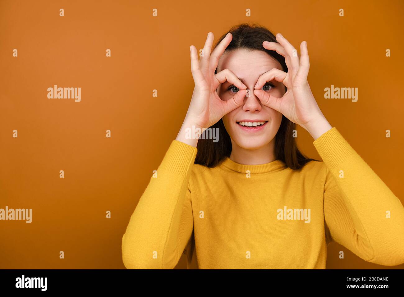 Funny smiling young woman having fun making glasses shape with hands ...