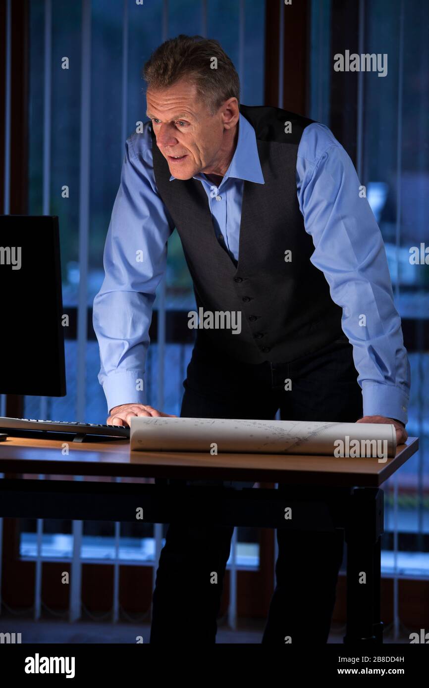 Senior architect or engineer standing at his desk looking at computer ...