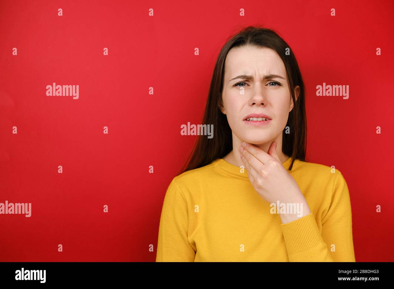 Tired young female model has sore throat, being sick and unwell, frowns ...