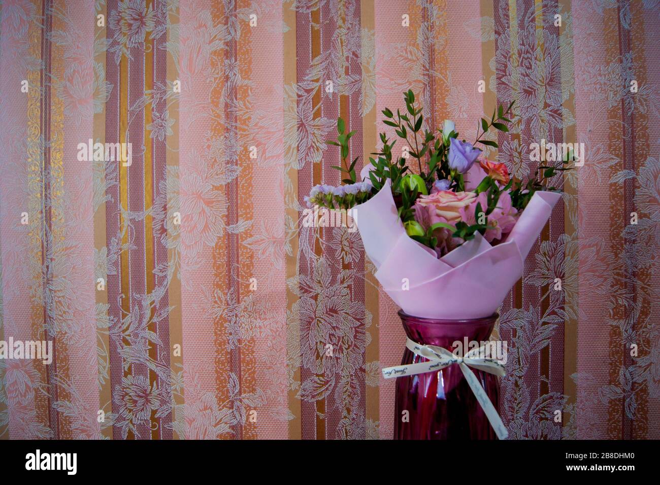 A delicate bouquet of different flowers in a light pink wrapper stands ...