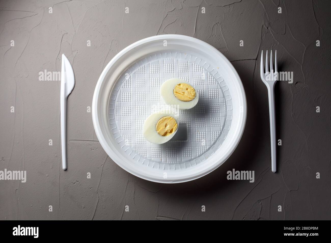 cut egg in a disposable plate with a fork and knife on a concrete ...