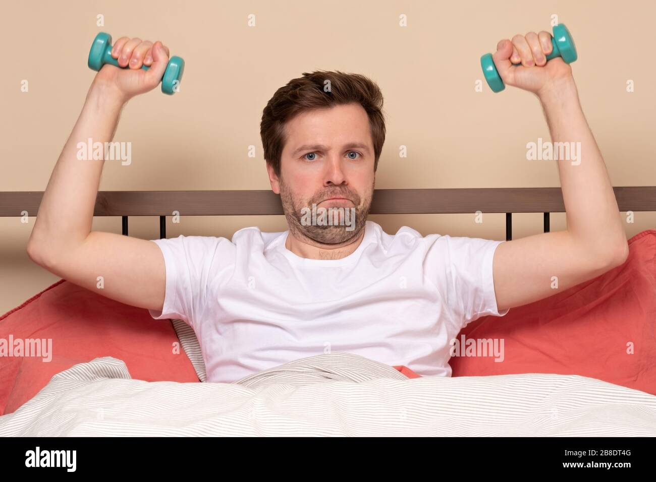 Handsome young man doing dumbbell front raises while exercising at home ...