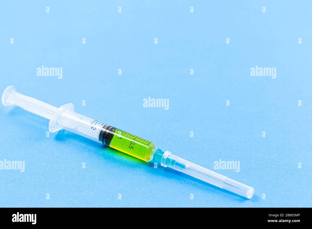 Green liquid in a syringe on a blue background, concept of Covid-19l ...