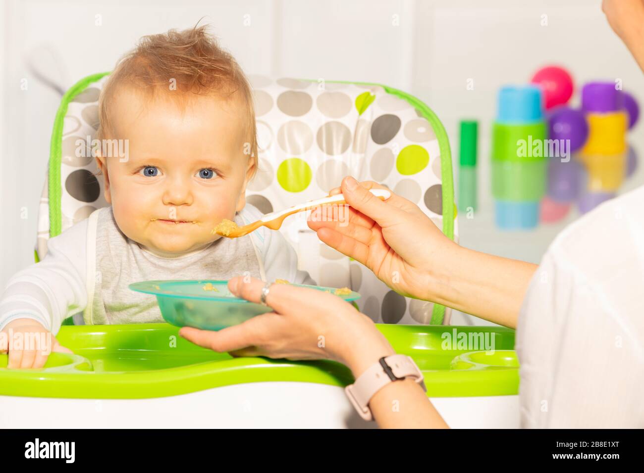 Portrait of happy baby toddler boy eating food with mother from plastic ...