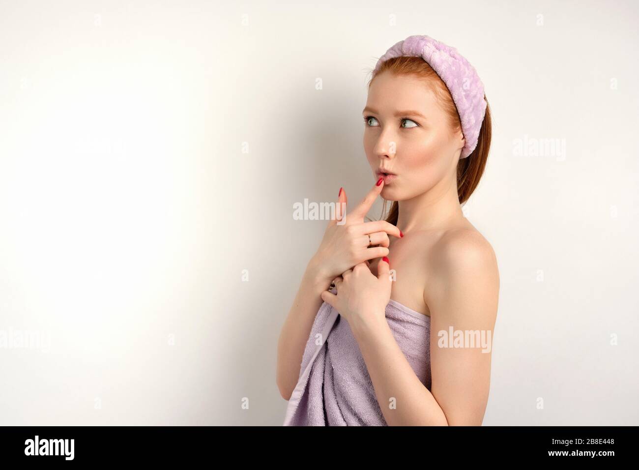 A red-haired girl with clean skin in a towel stands on a white ...