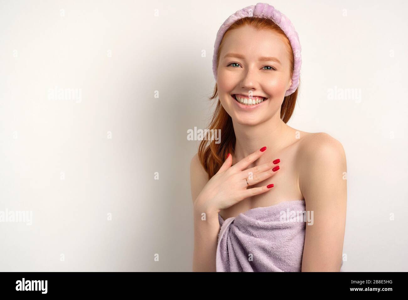 The red-haired girl with clean skin in a towel stands on a white ...