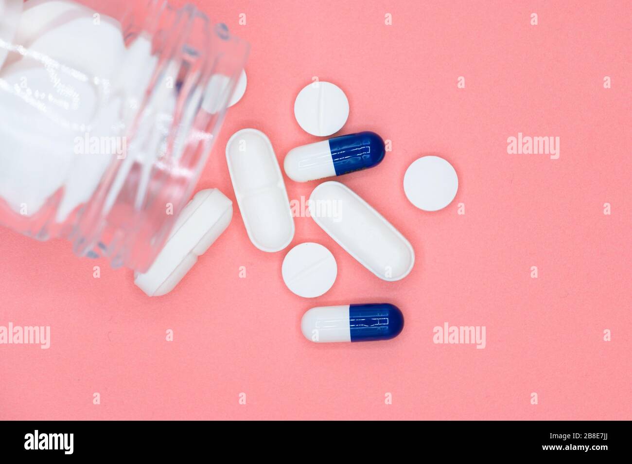Close up of Pills spilling out of pill bottle on pink background. with ...