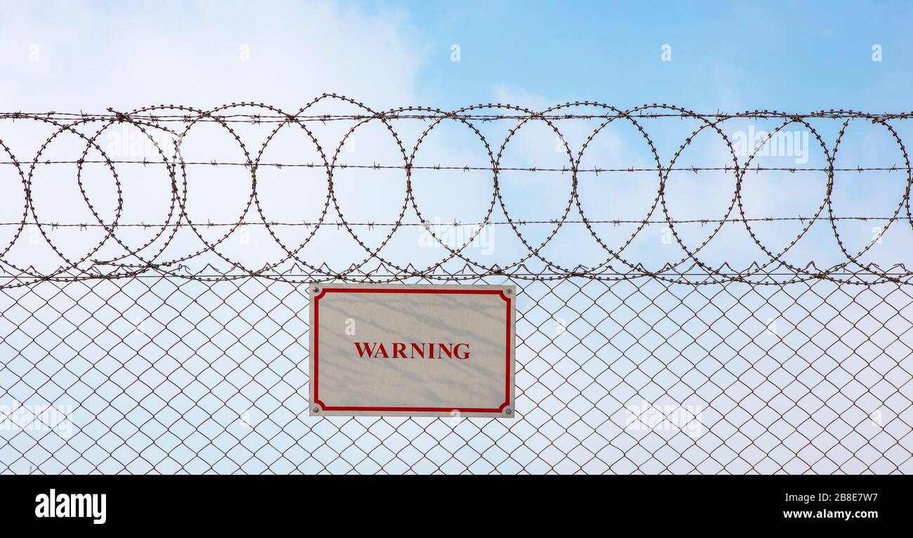 Warning sign hangs on a metal barbed wire fence ensuring safety and ...