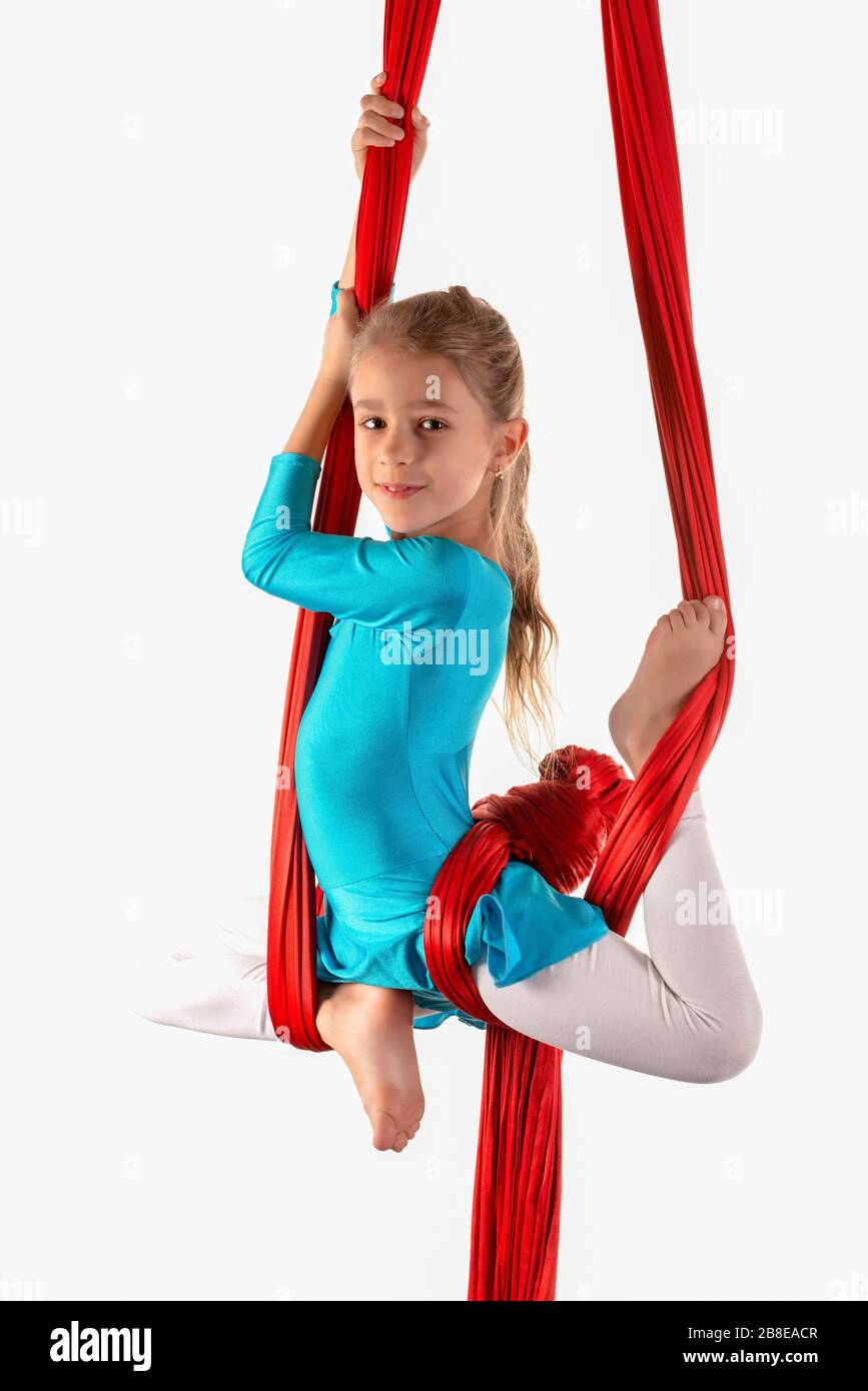Cheerful pretty little girl in a blue gymnastic suit does tricks in a ...