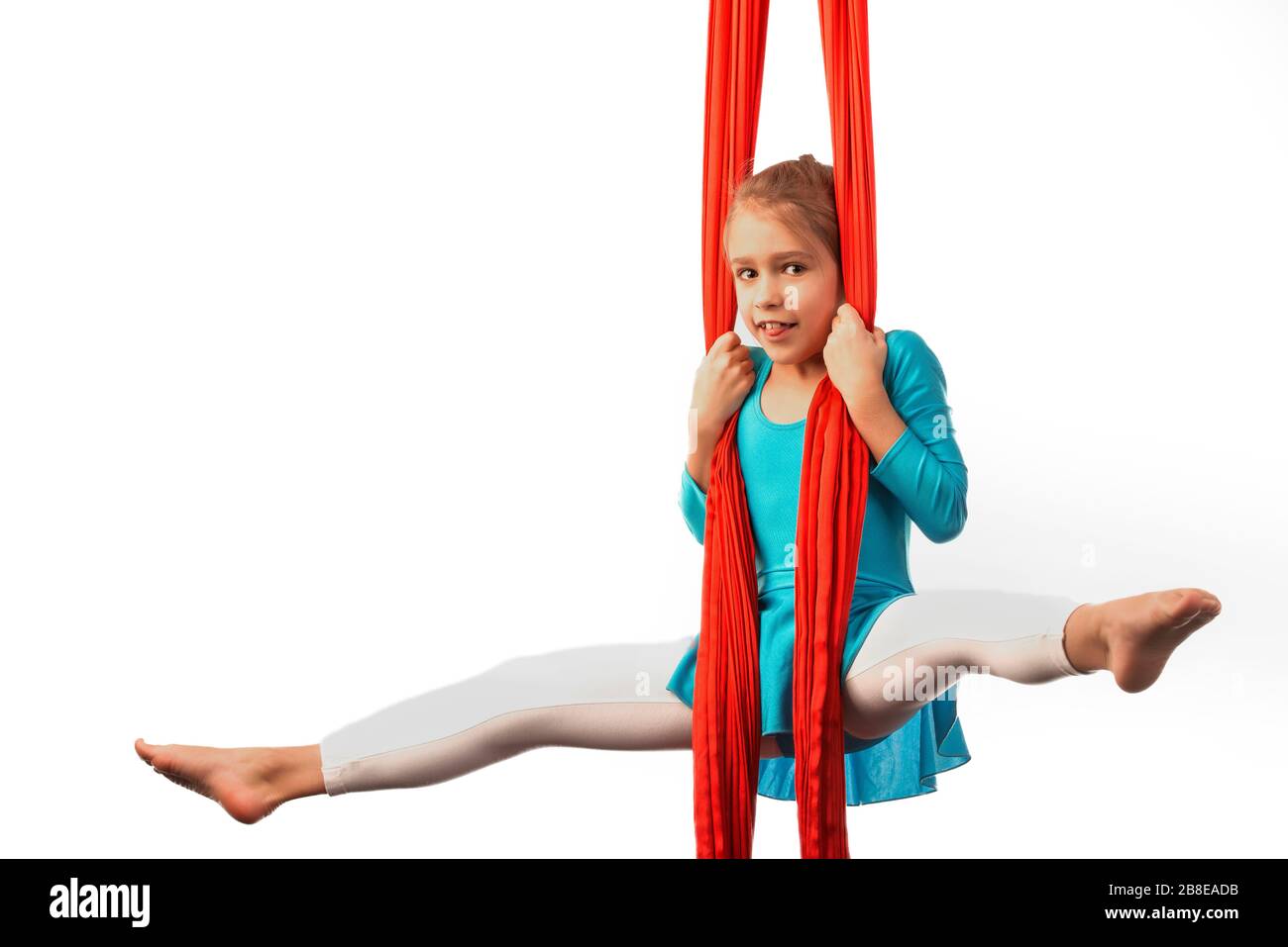 Little acrobat girl doing splits in the air holding on to a red air ...