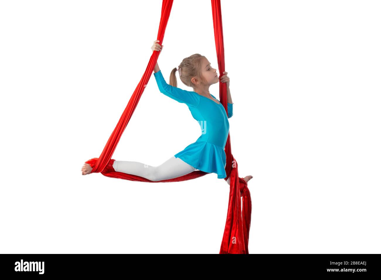 Little acrobat girl doing splits in the air holding on to a red air ...
