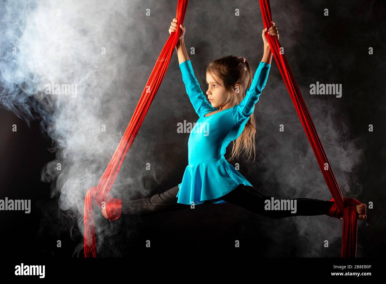 Focused little pretty girl in a blue gym suit does a splits in the air ...