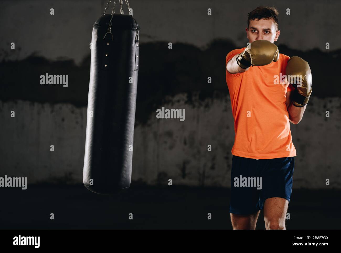 Strong kickboxer man punching black sand bag on gym background Stock ...