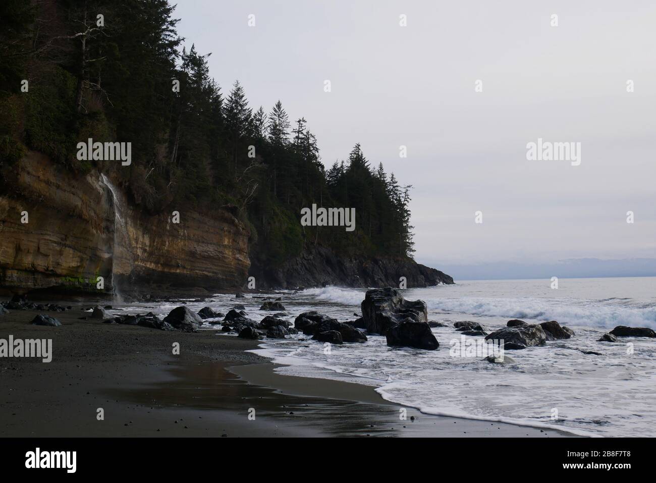 Empty Canadian beach with trees, cliff, waterfall, rocks and crashing ...