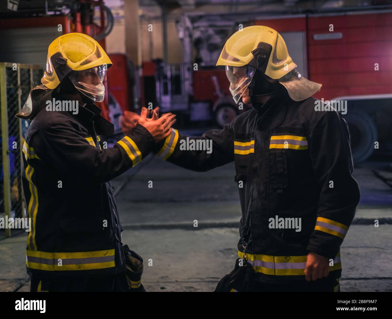 Portrait of two young firemen in uniform standing inside the fire ...