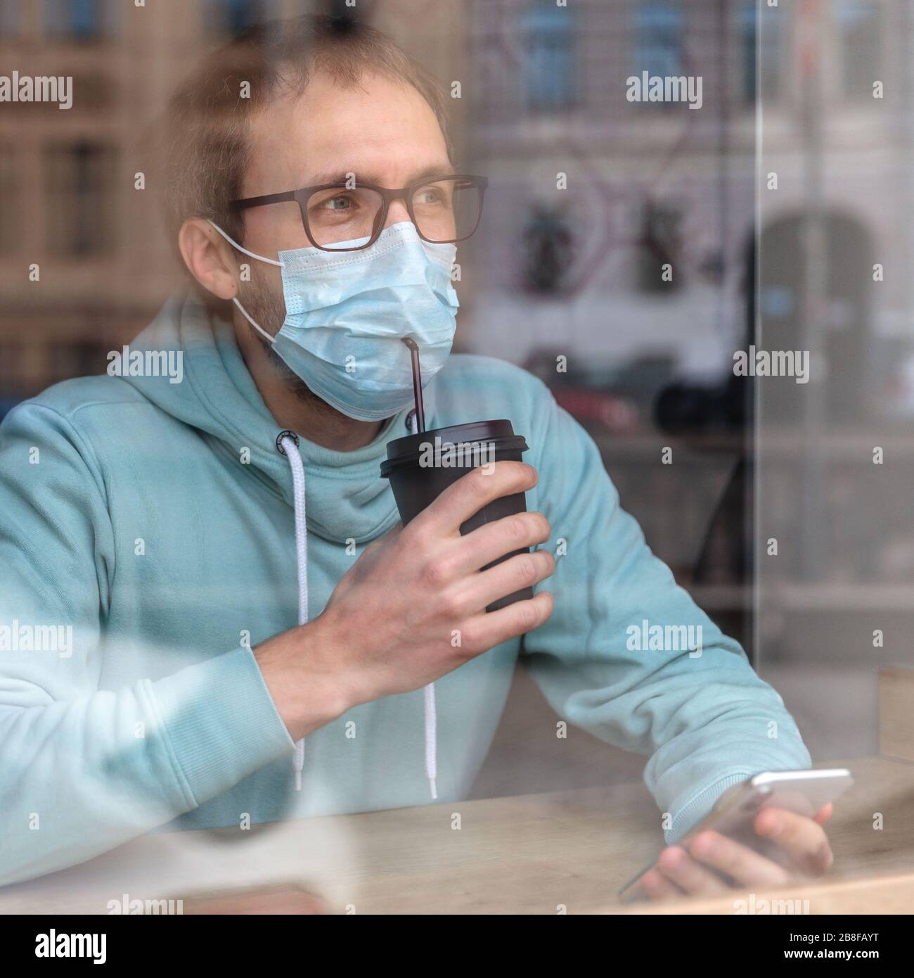 Man wearing protective mask, drinking coffee through a straw in a mask ...