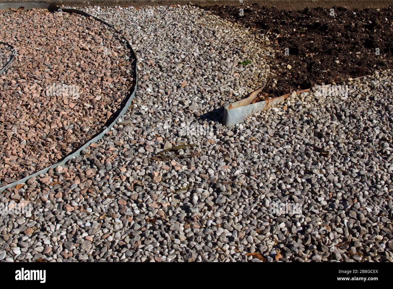 Metal edging separating dirt and different colors of gravel in a park ...