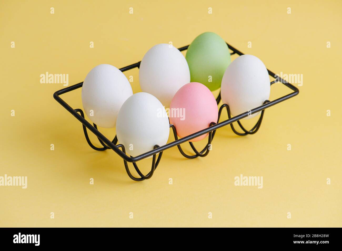 Colorful easter eggs and regular ones on a metal egg holder over yellow ...