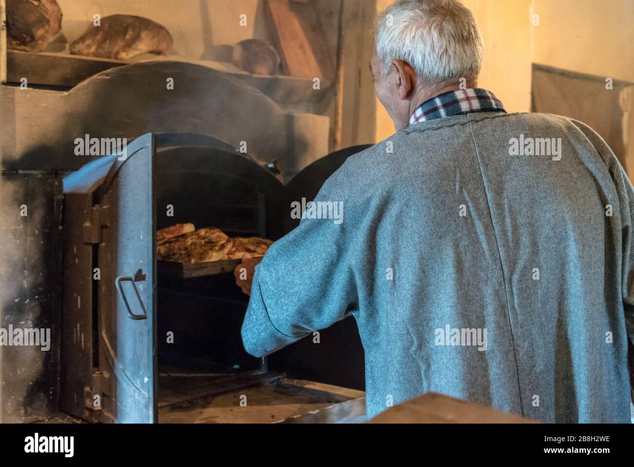 Traditional baker checking the bread in his vintage oven in the village ...