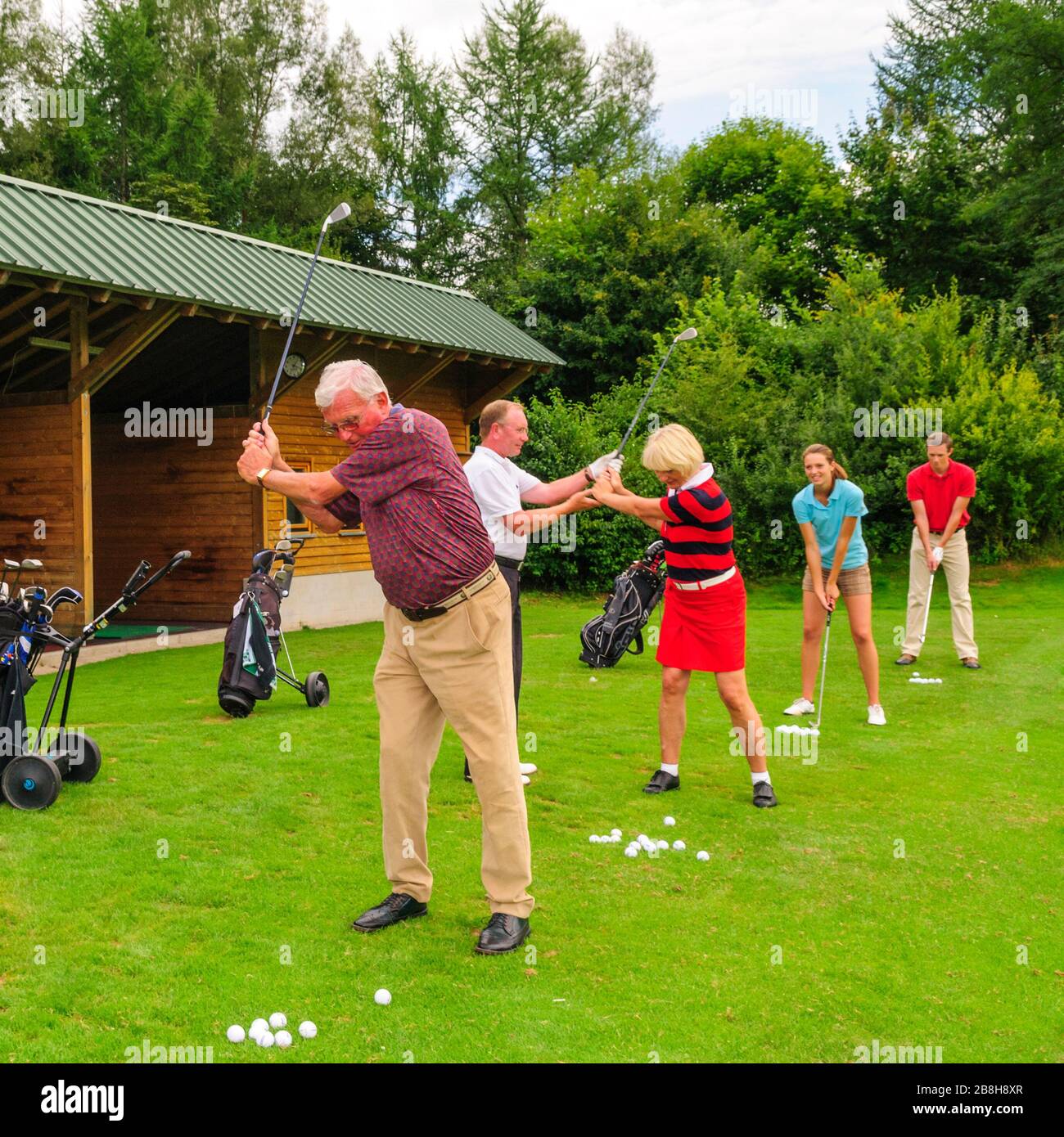 Golf players practising with golf pro on drivingrange Stock Photo - Alamy