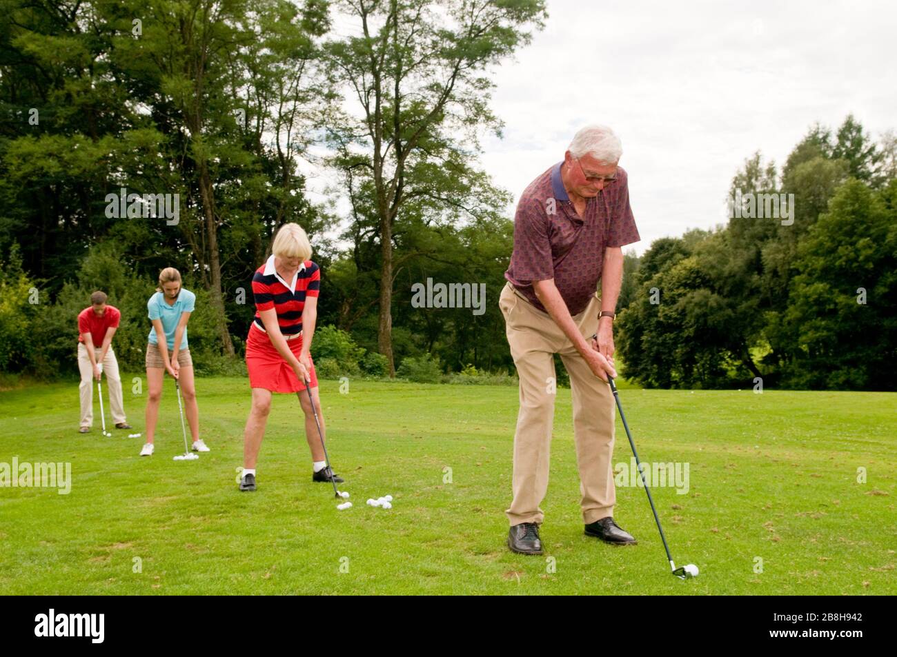 Golf players practising with golf pro on drivingrange Stock Photo - Alamy