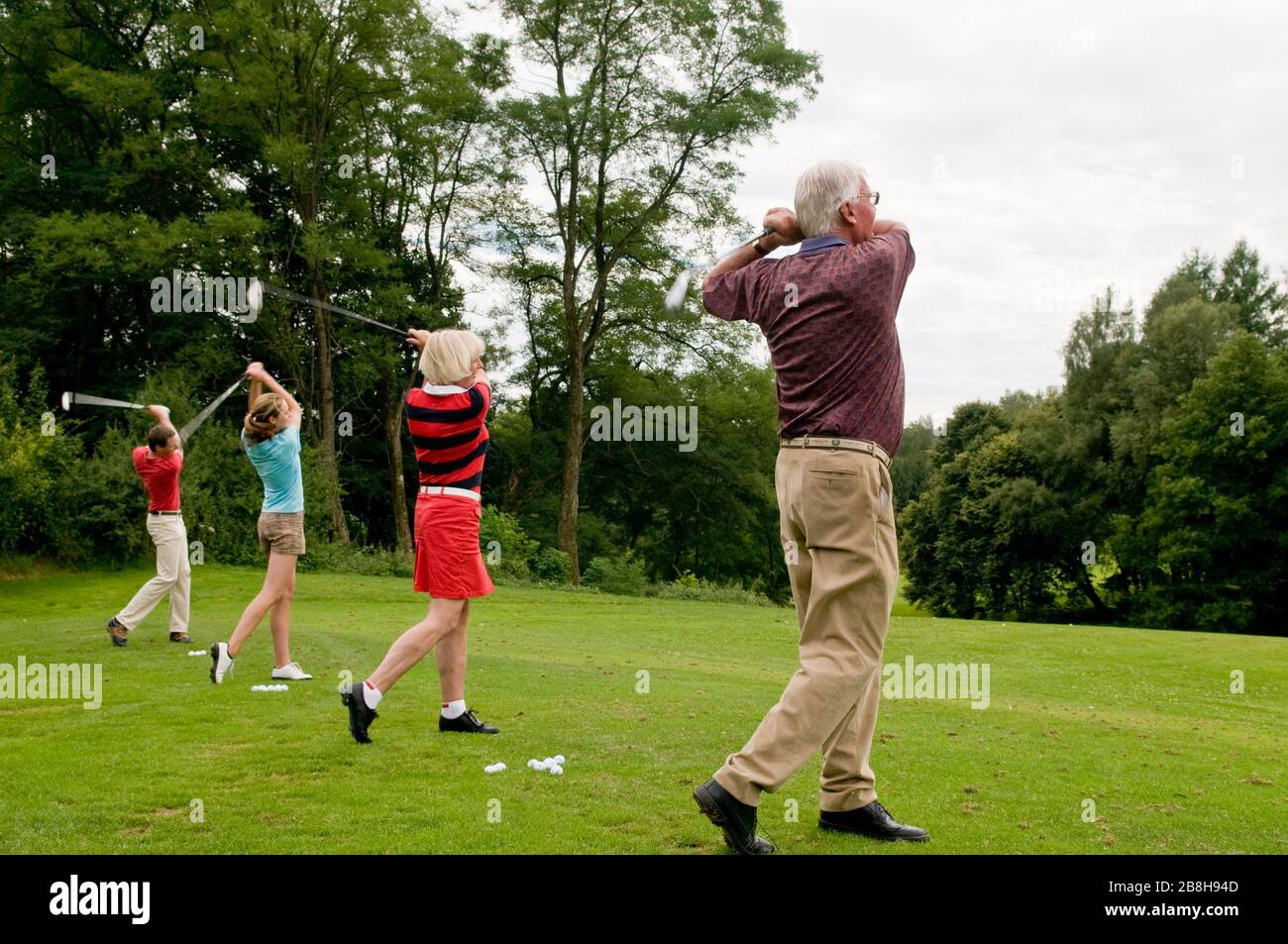 Golf players practising with golf pro on drivingrange Stock Photo - Alamy