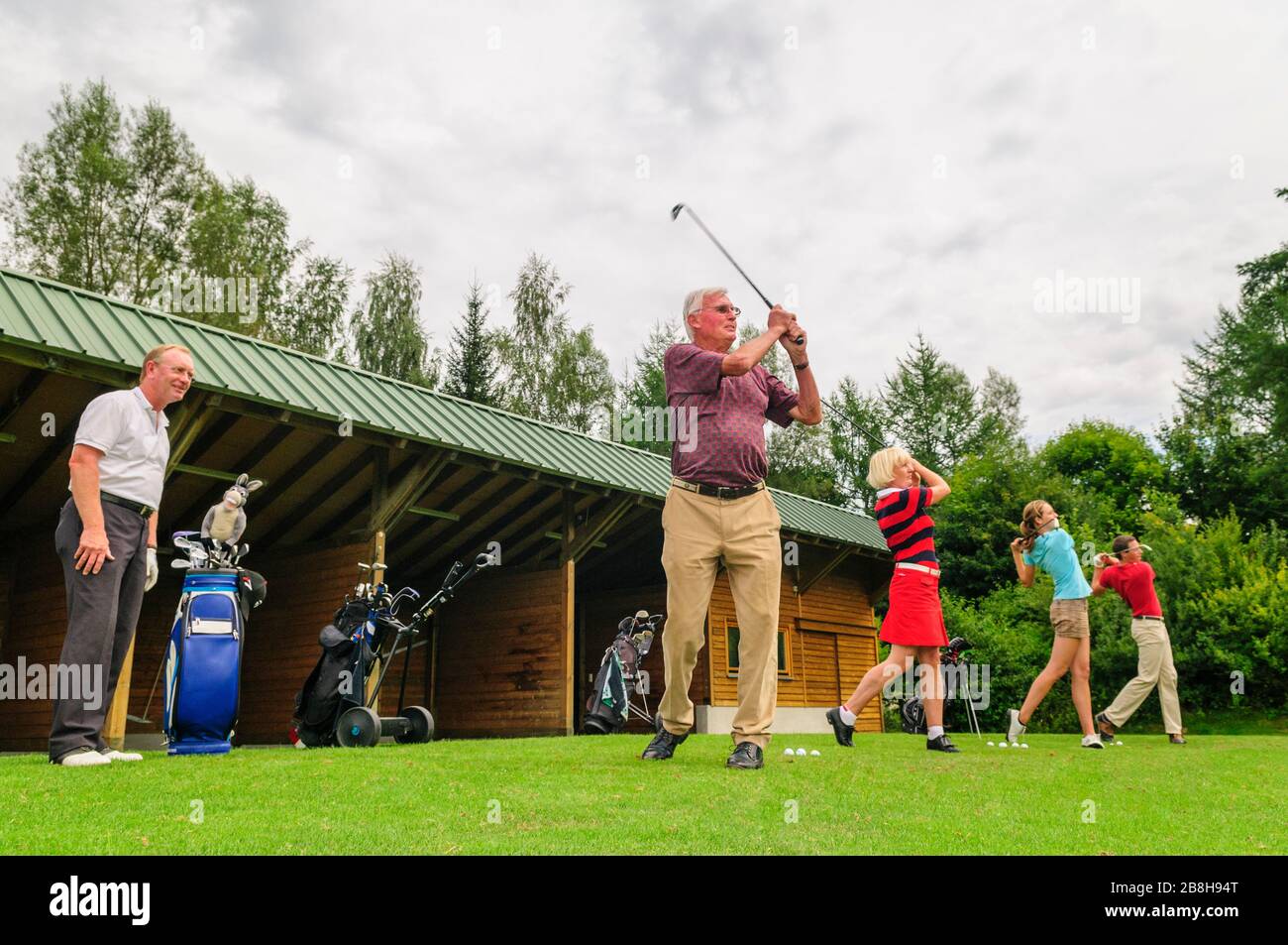 Golf players practising with golf pro on drivingrange Stock Photo - Alamy