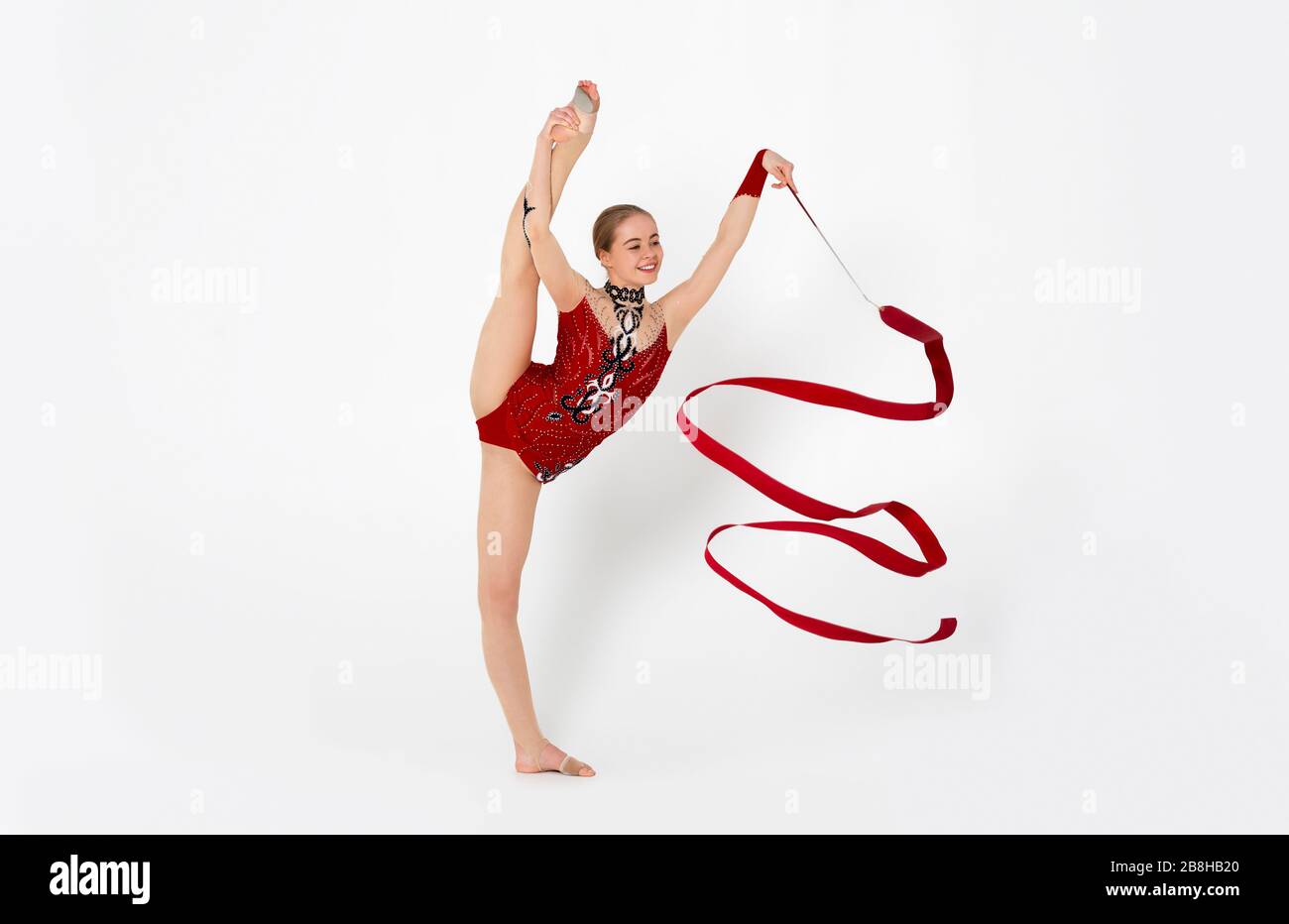 Smiling millennial gymnast with ribbon working out on white background ...