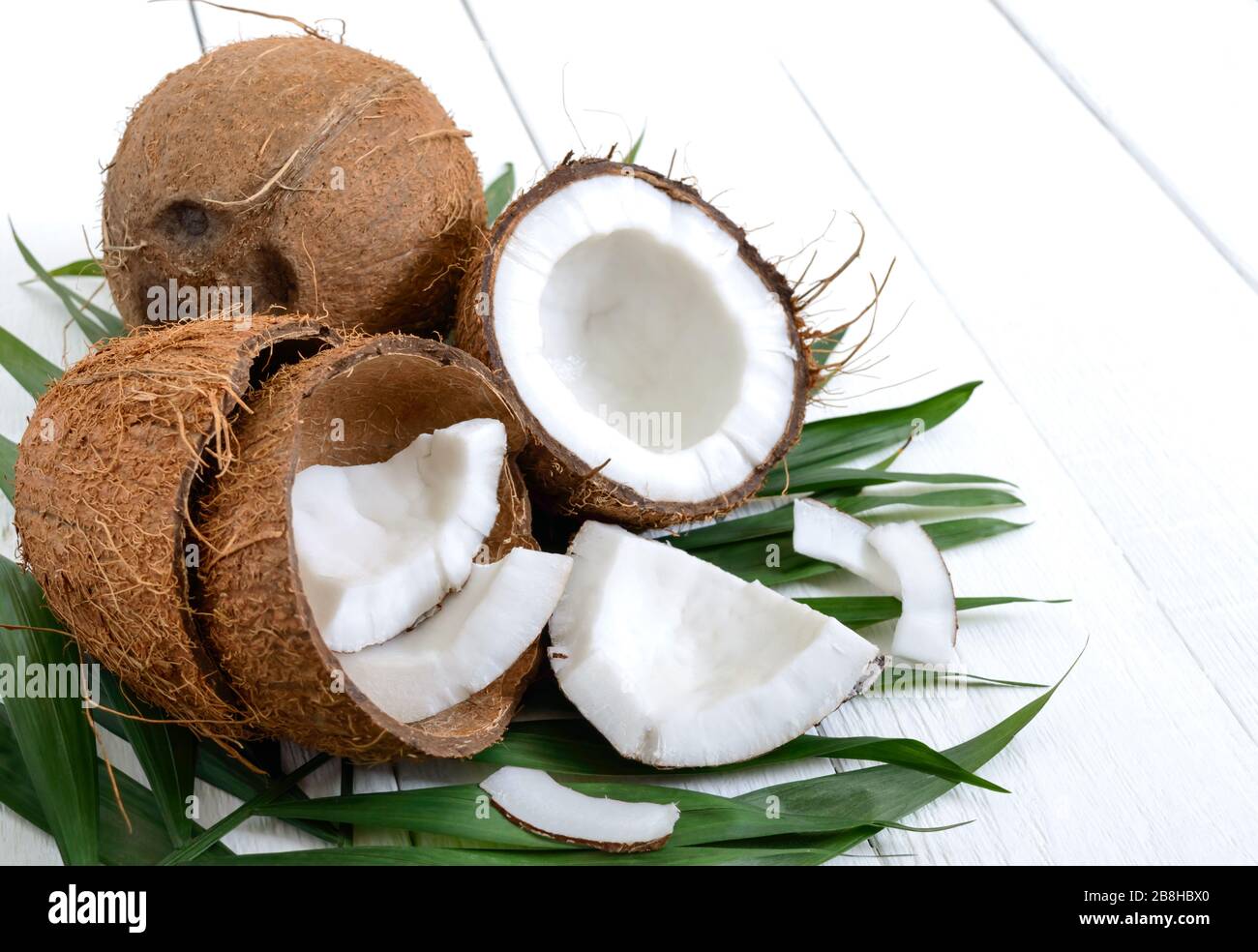 Coconut. Whole coconut, shell and green leaves on a white wooden ...