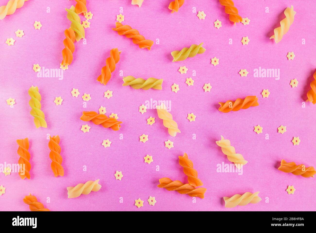 Raw colored fusilli and Stellini pasta scattered on pink background ...