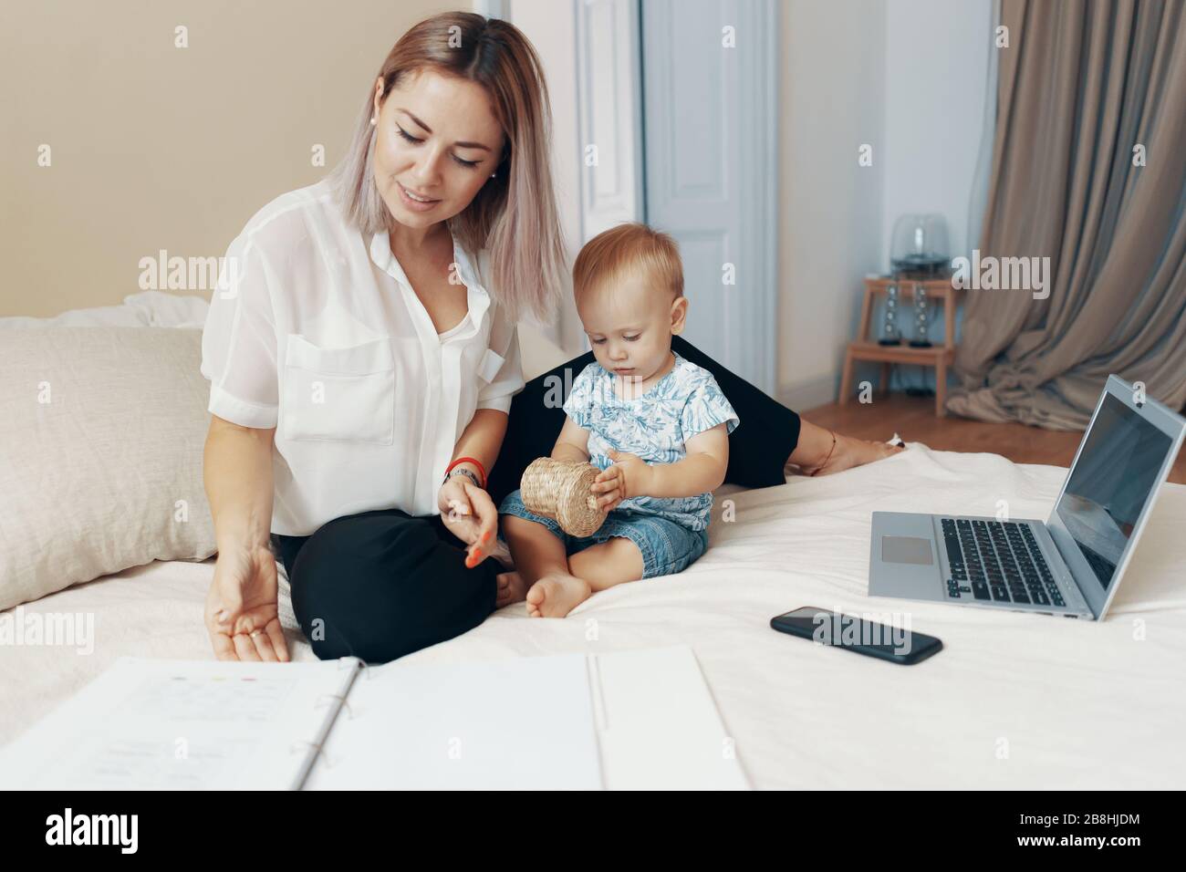 Young mother with her child working in bedroom at home. Multi-tasking ...