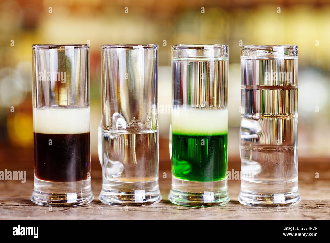 Multi-layered alcoholic cocktails are displayed in a row on the bar ...