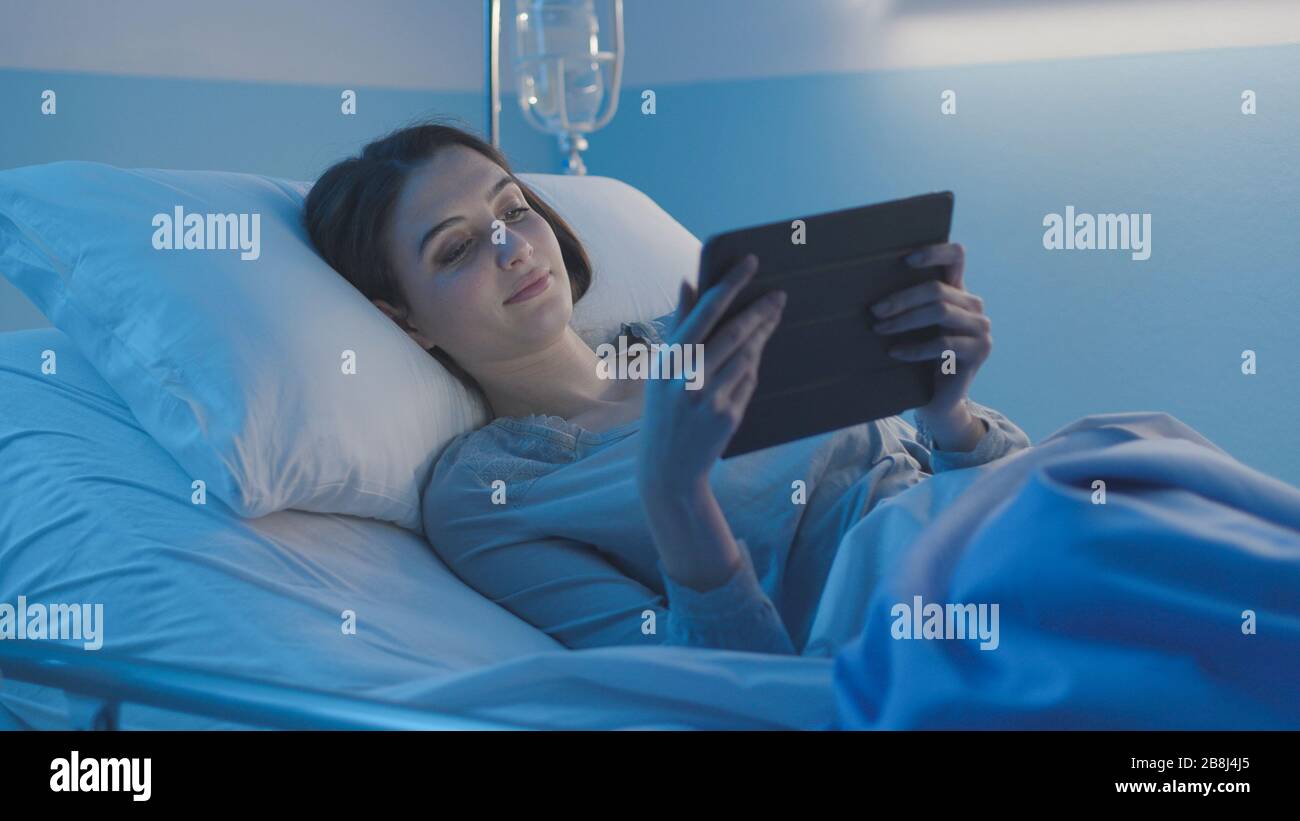 Young smiling patient lying in a hospital bed at night and connecting ...