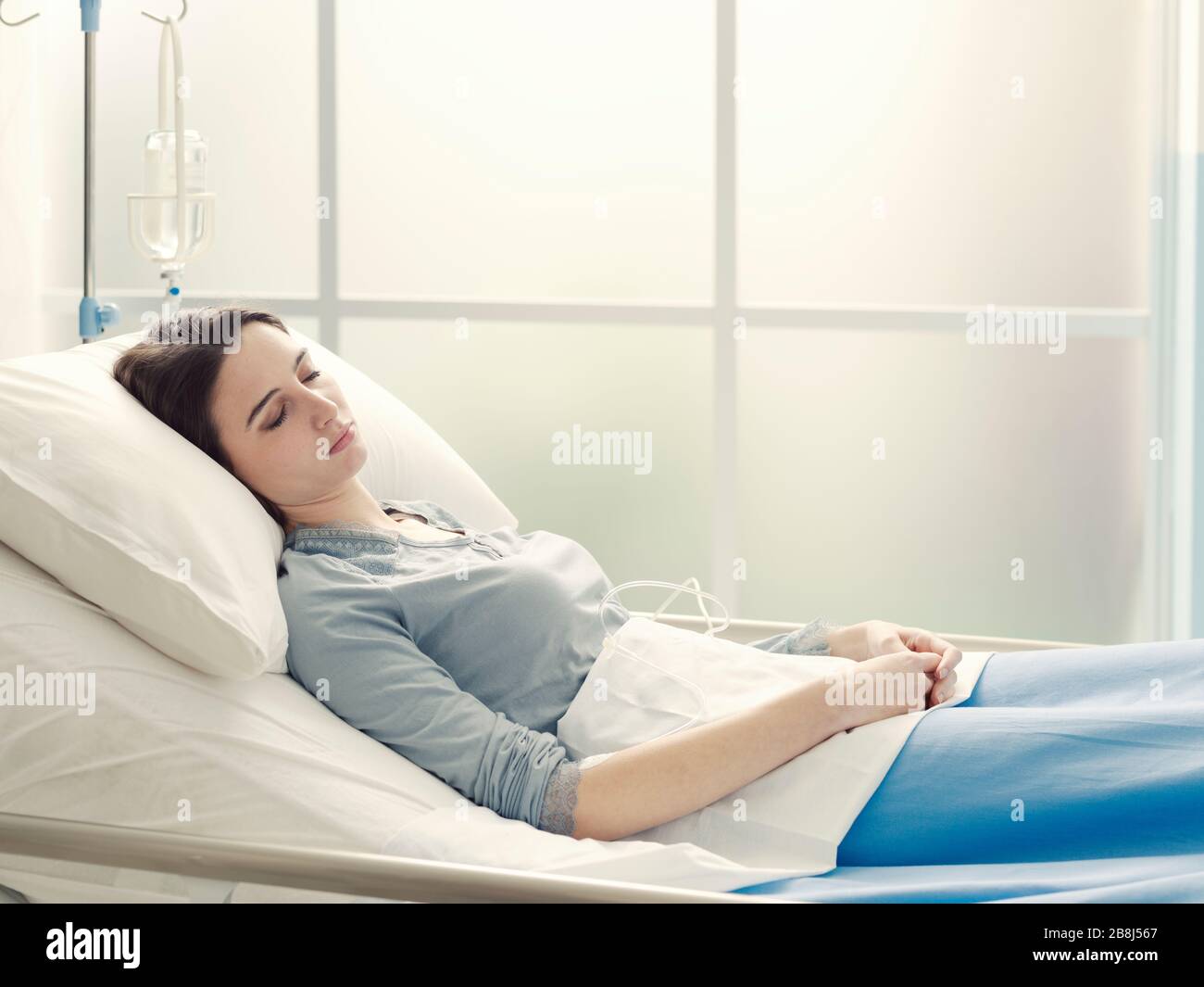 Young female patient lying in bed with IV drip, medicine and treatment ...