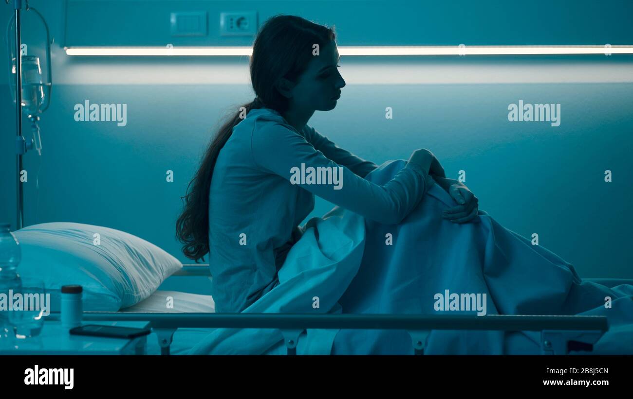 Sad female patient lying in the hospital bed at night, she is sleepless ...