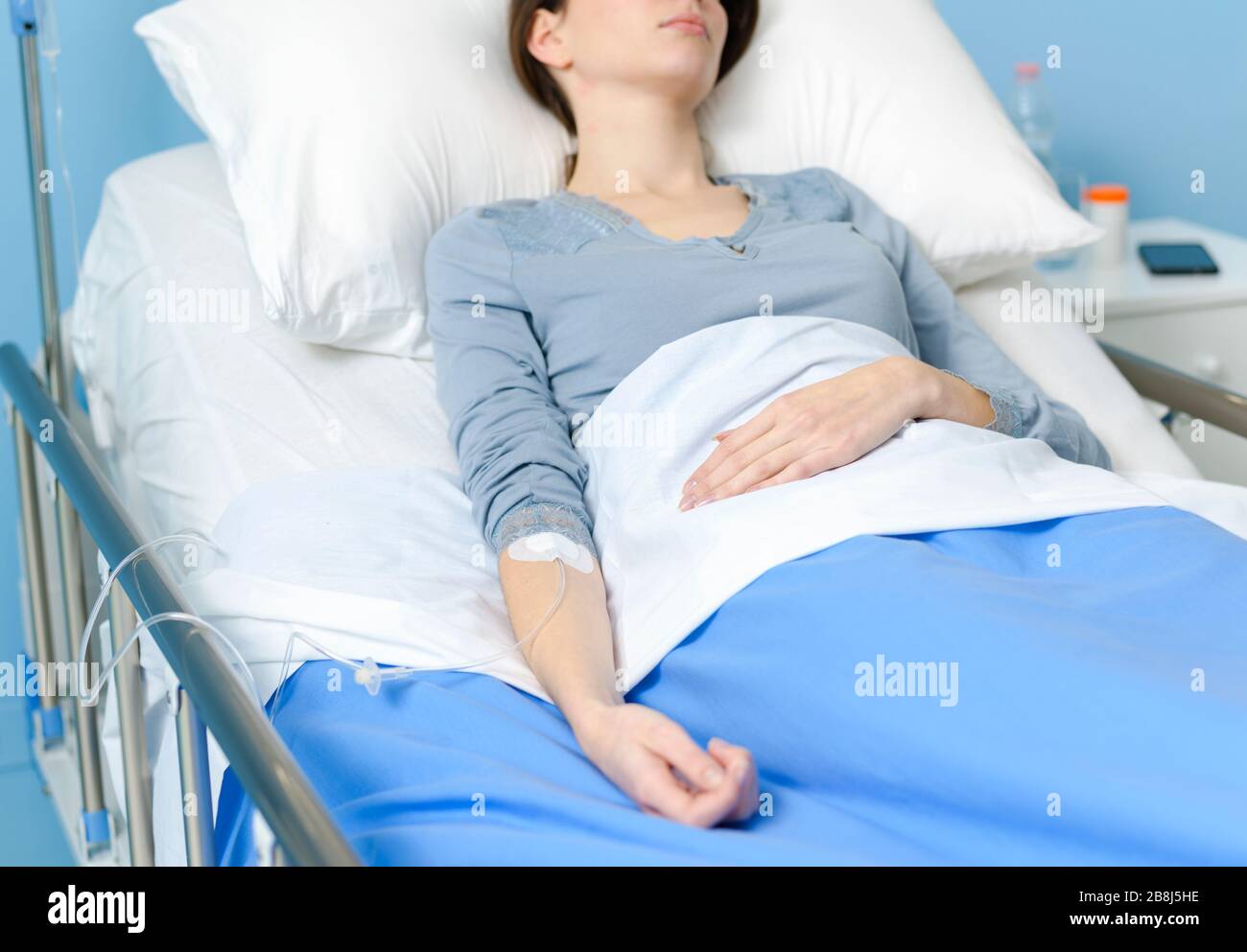 Young female patient lying in bed with IV drip, medicine and treatment ...