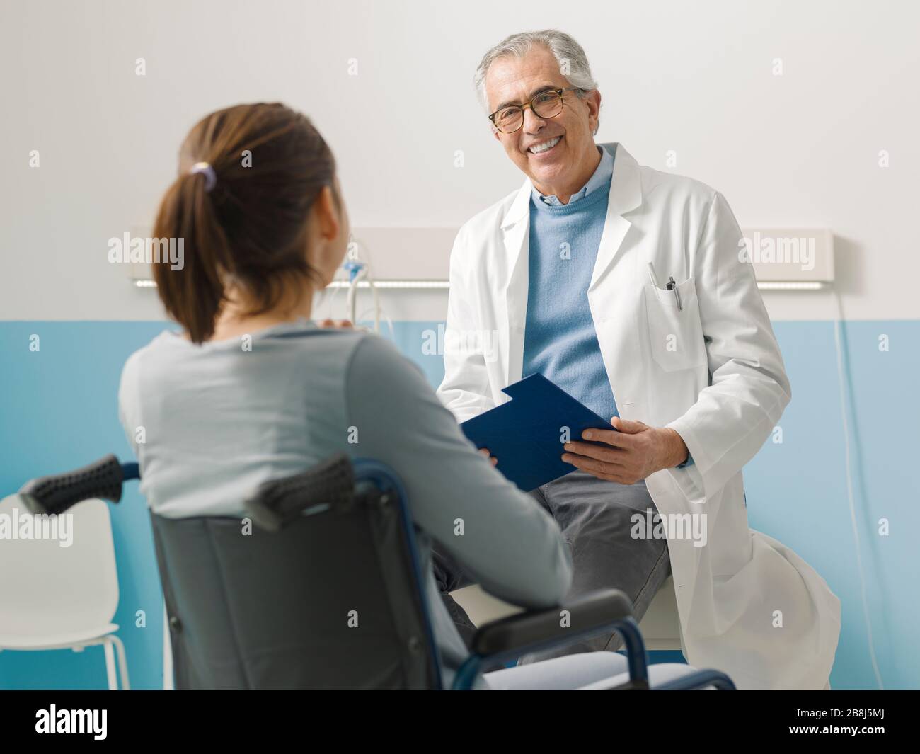 Confident doctor visiting a paraplegic patient in wheelchair at the ...