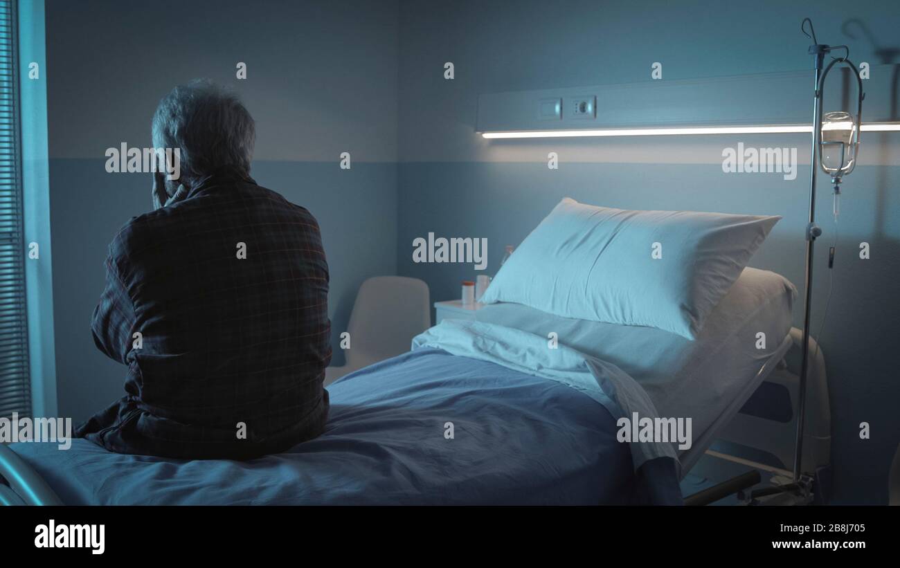 Sad lonely senior sitting in a hospital bed back view, senior care and ...