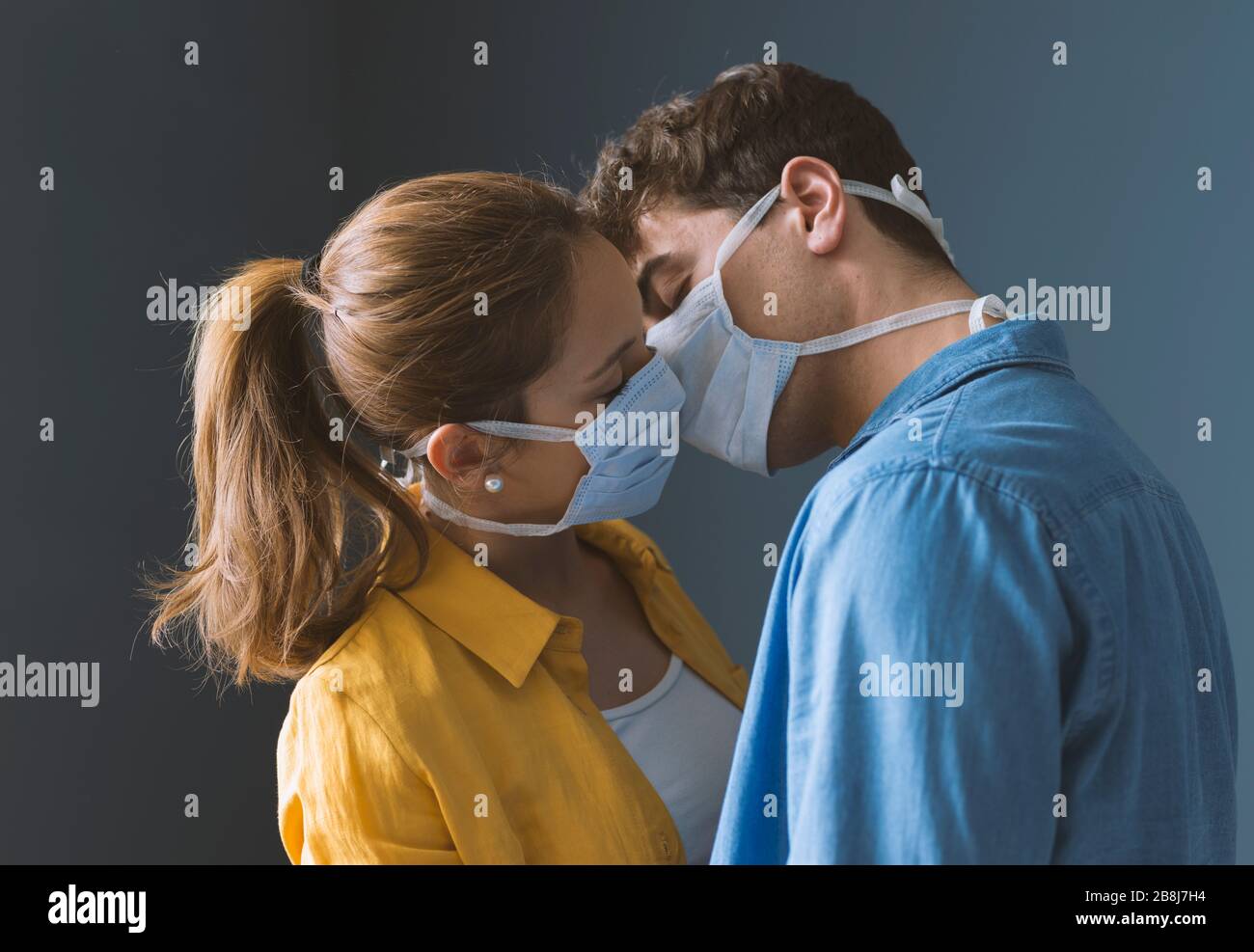 Young millennials couple wearing protective face masks and kissing each ...