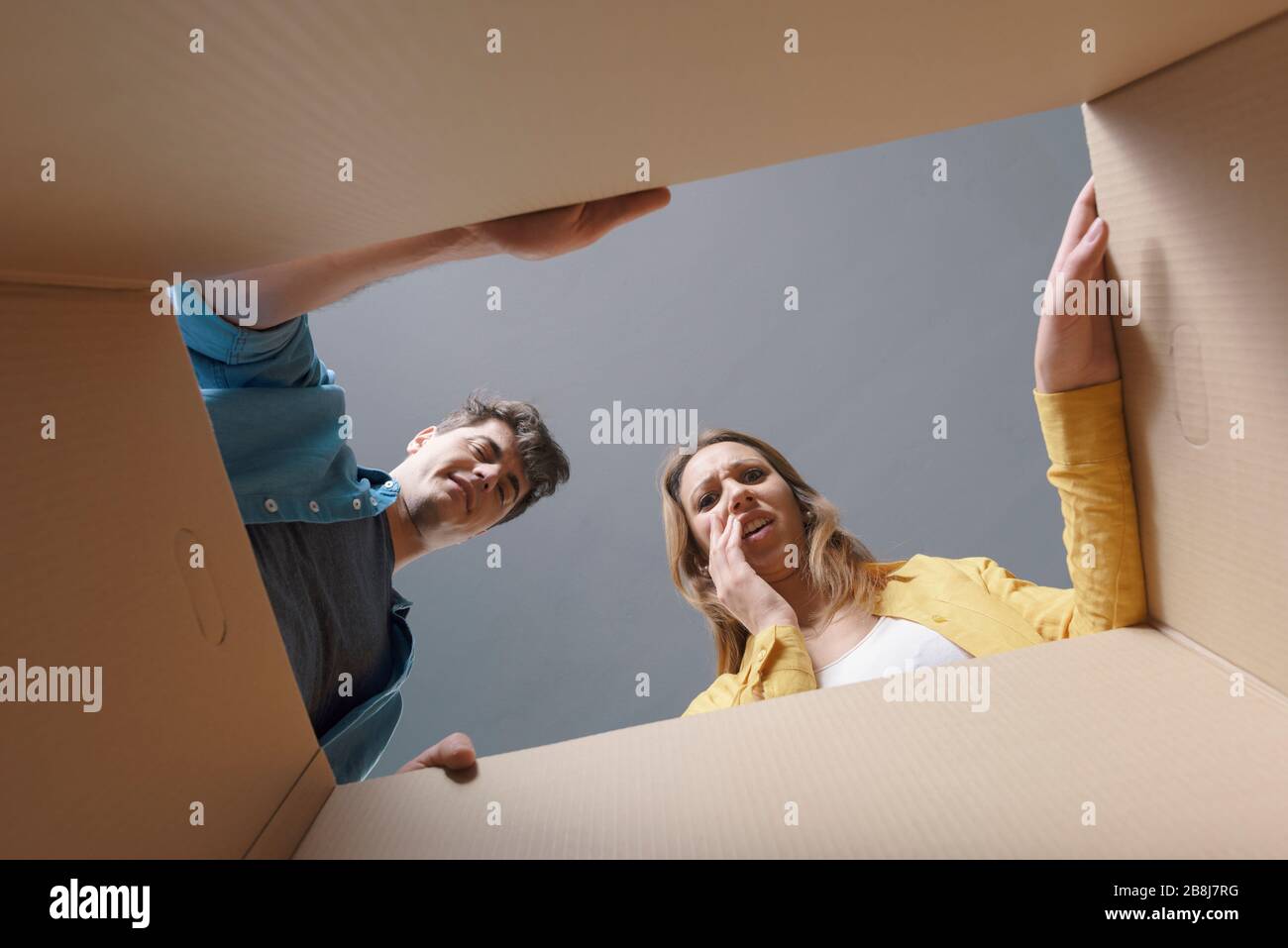 Happy couple opening a cardboard box and looking inside, they are ...