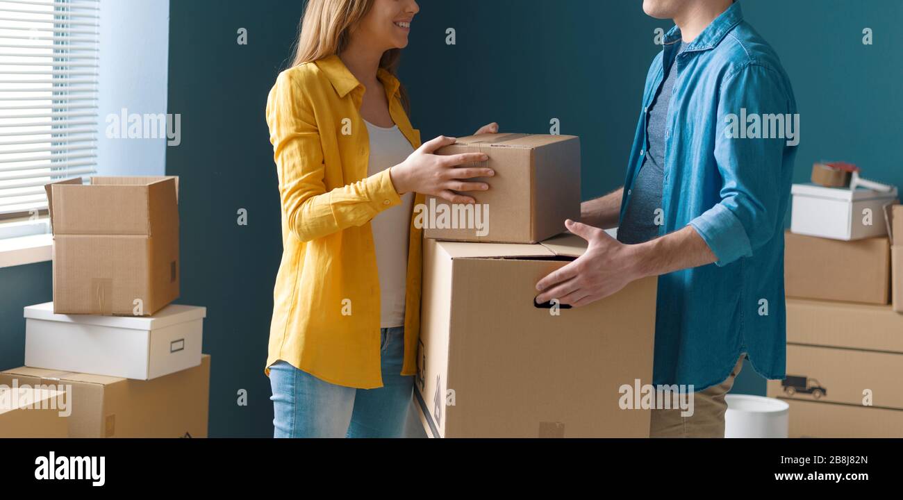 Happy couple moving in their new house: the man is carrying a box and ...